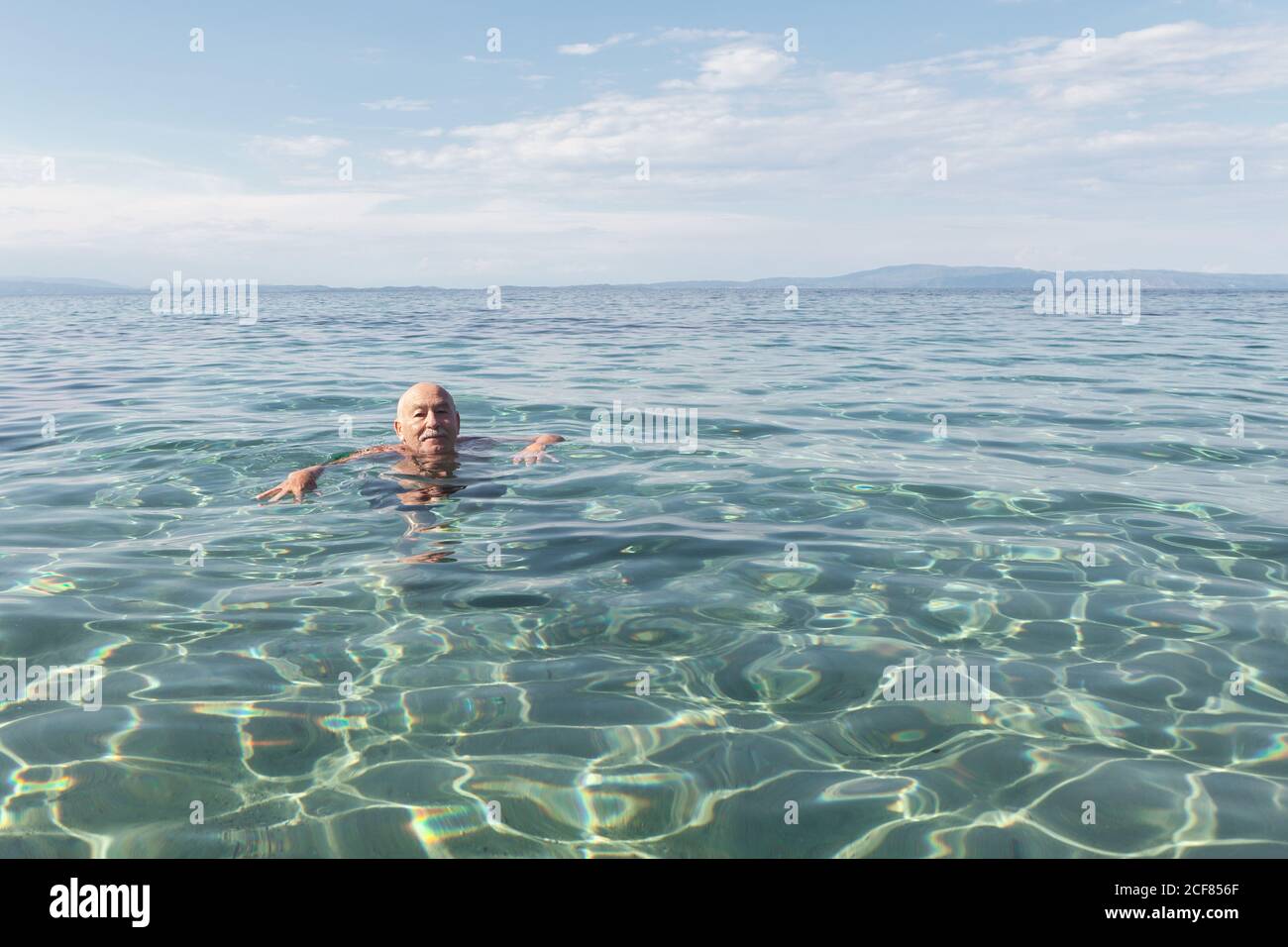 Elderly retired man floating in crystal water enjoying tropical weather ...