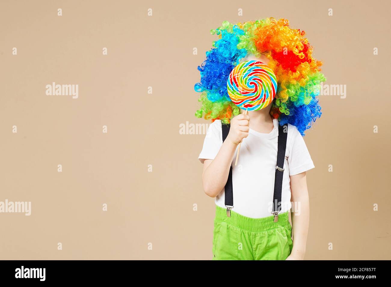 Happy clown boy in large colorful wig. Let's party! Funny kid clown. 1 ...