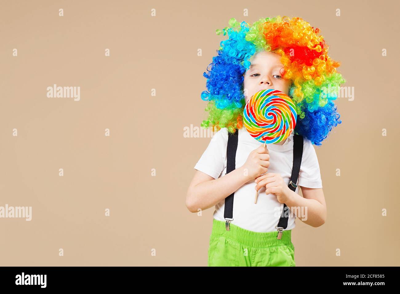 Happy clown boy in large colorful wig. Let's party! Funny kid clown. 1 ...