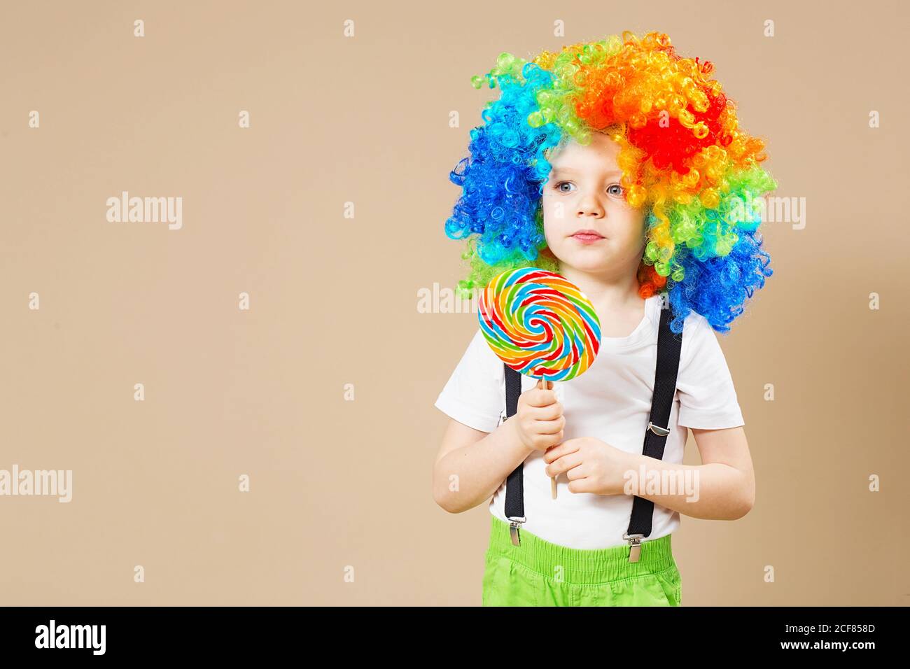 Happy clown boy in large colorful wig. Let's party! Funny kid clown. 1 ...