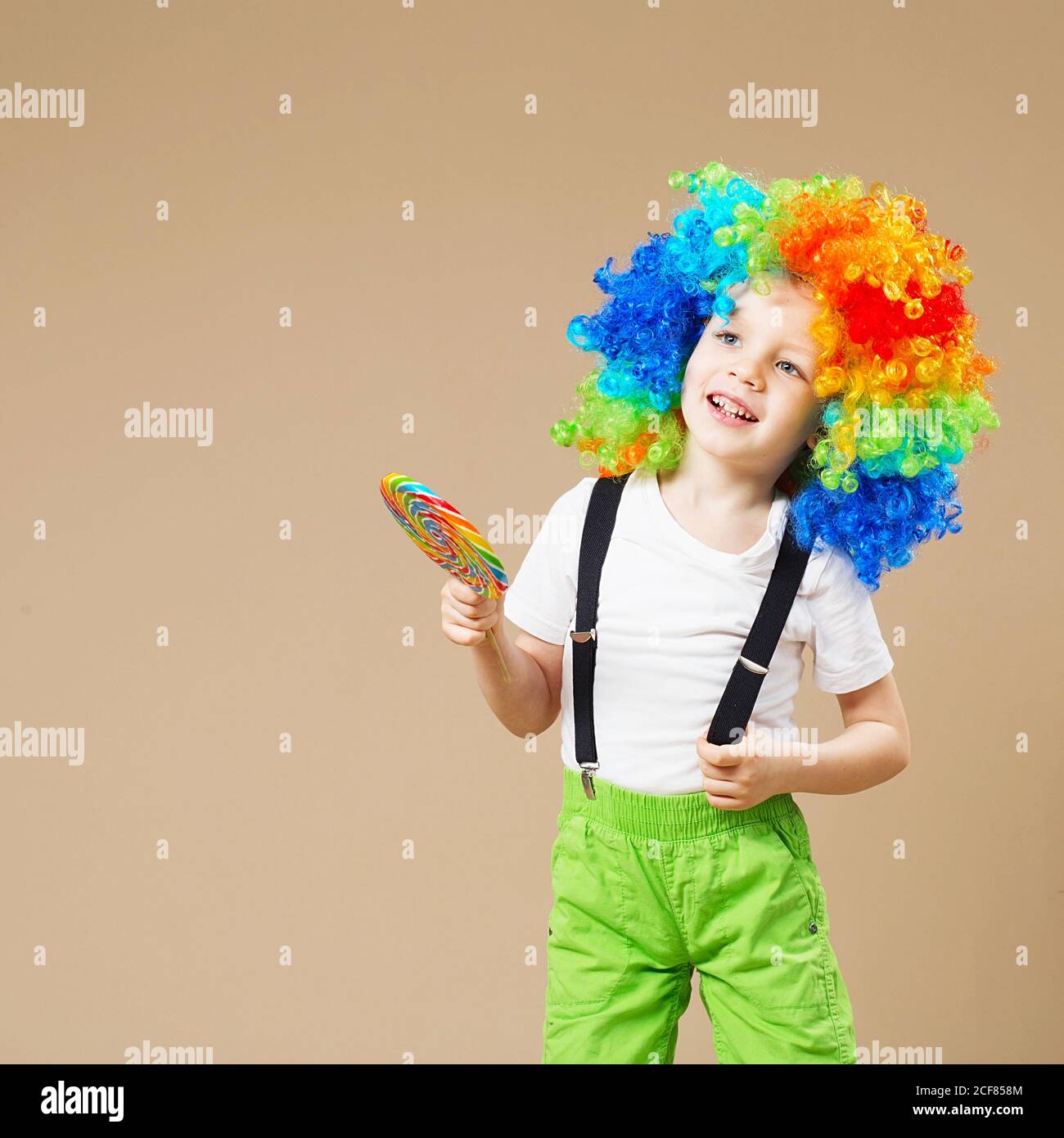 Happy clown boy in large colorful wig. Let's party! Funny kid clown. 1 ...