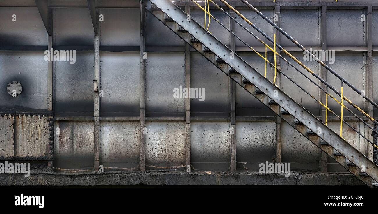 Metal staircase in spacious industrial workshop near shabby metal wall ...