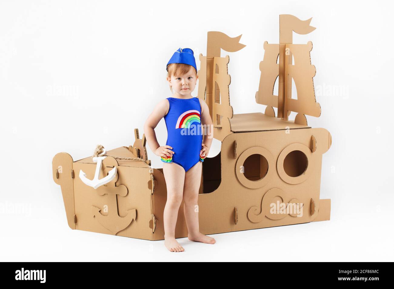 Cute Little girl wearing bright swimsuit playing with cardboard ship on ...