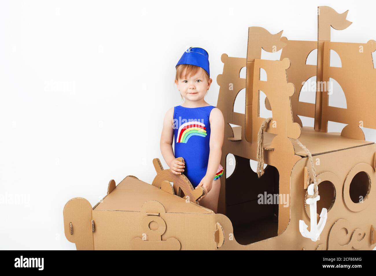 Cute Little girl wearing bright swimsuit playing with cardboard ship on ...
