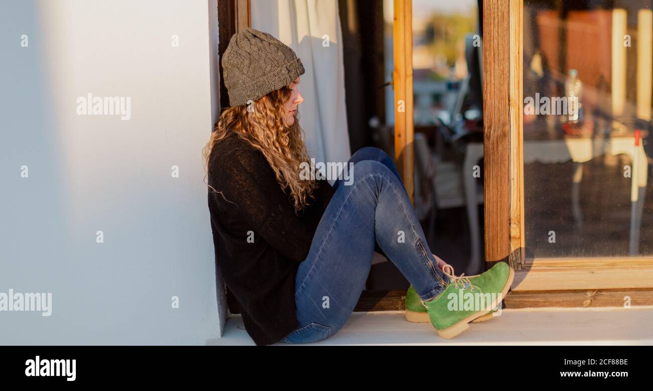Side view of melancholic young female with long curly hair in casual ...
