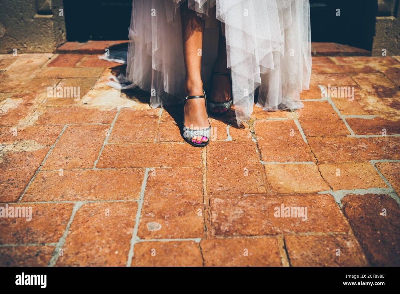 Crop bride in white wedding dress dancing near entrance of old building ...