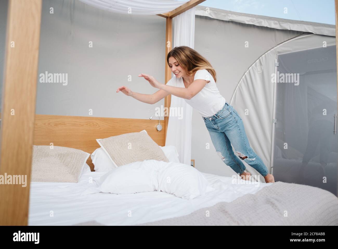 Happy young Woman falling on bed with white linen in big tent with ...