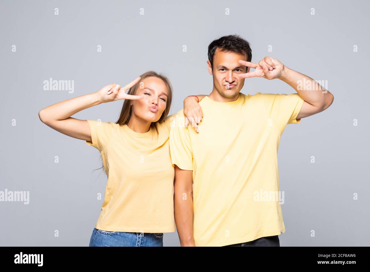 Lovely couple showing peace symbol near their eyes, standing isolated ...