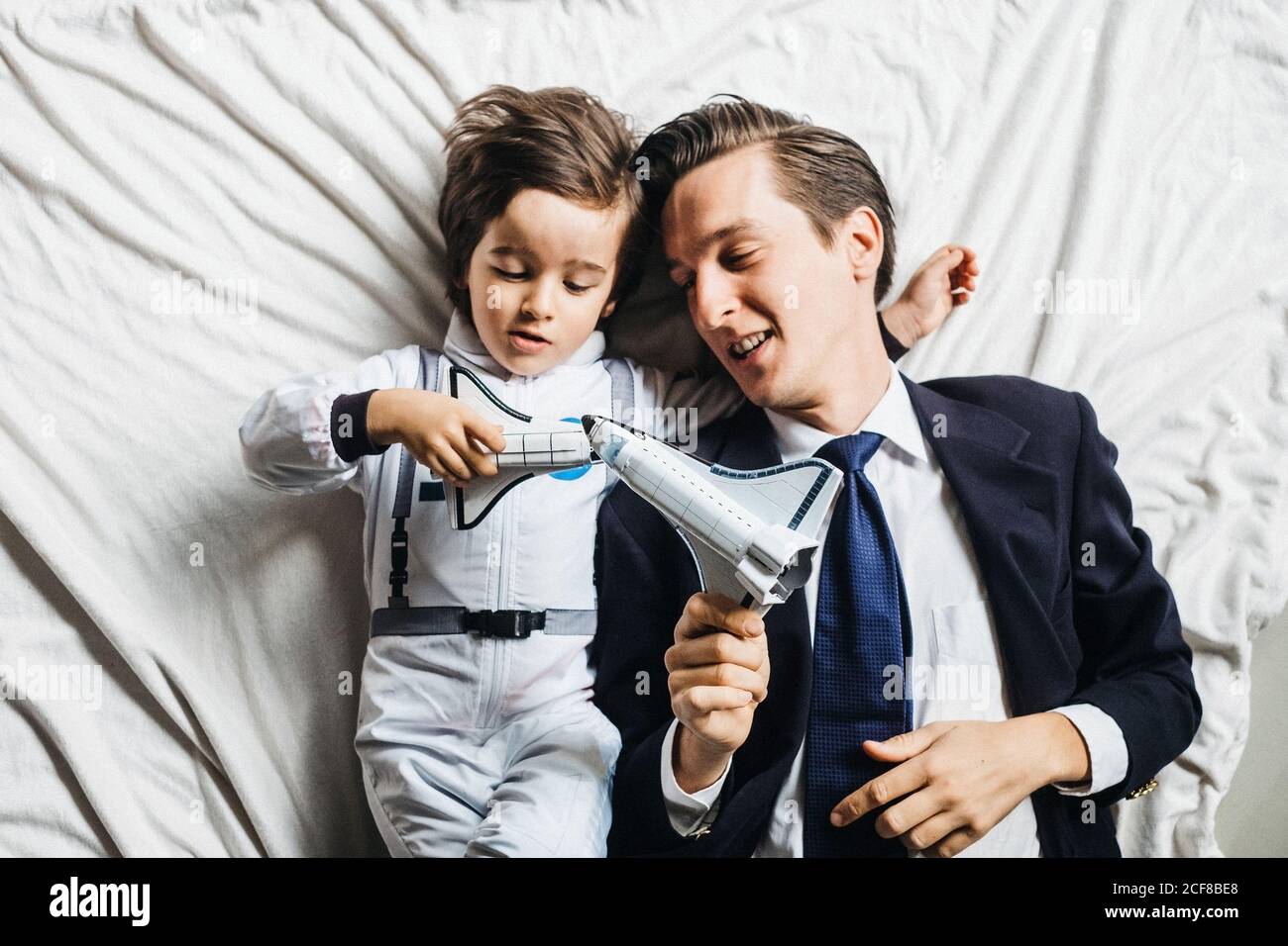 From above of cheerful boy in astronaut costume and dad in formal suit ...