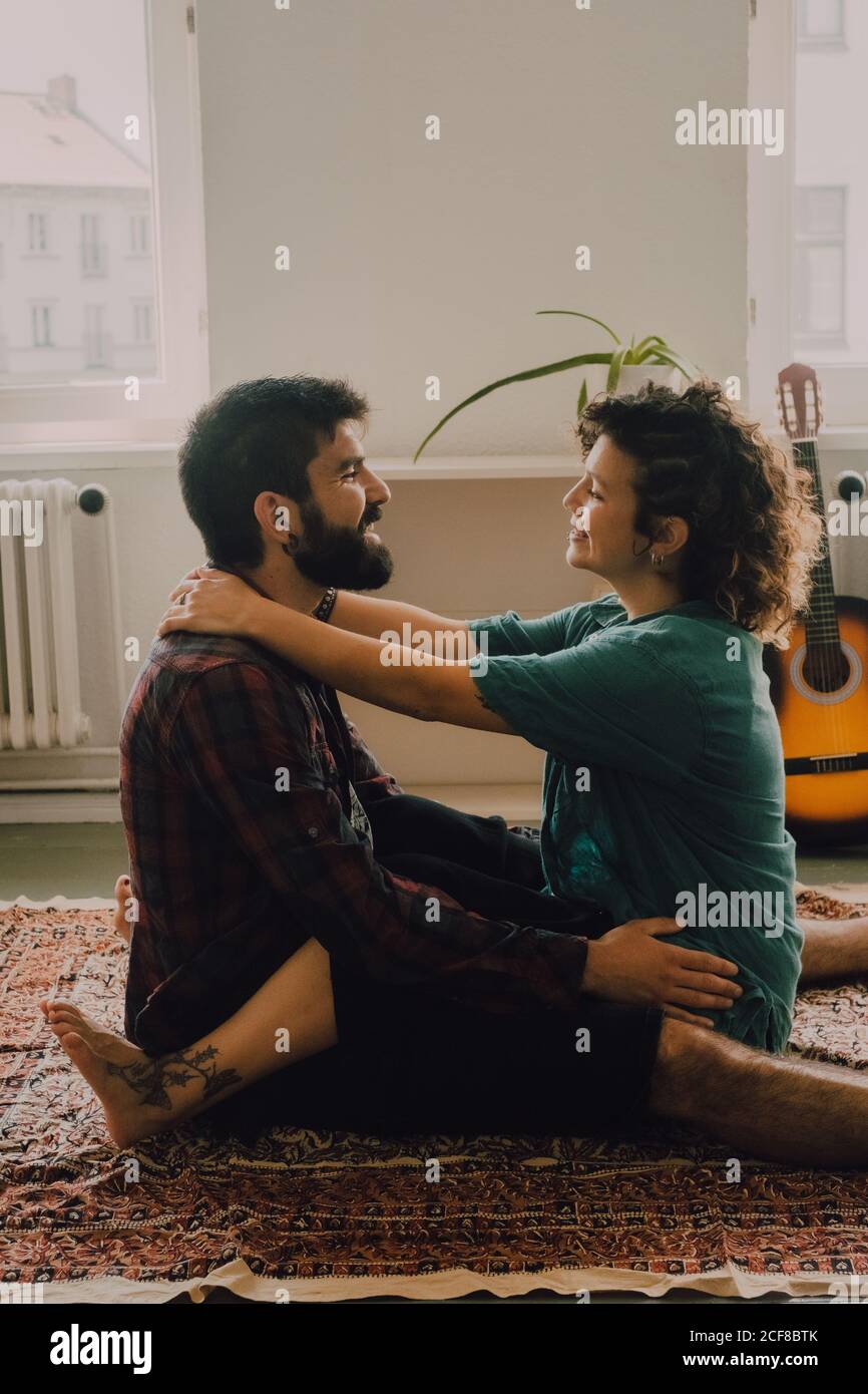 Side view of tender couple in casual clothes cuddling and smiling while ...