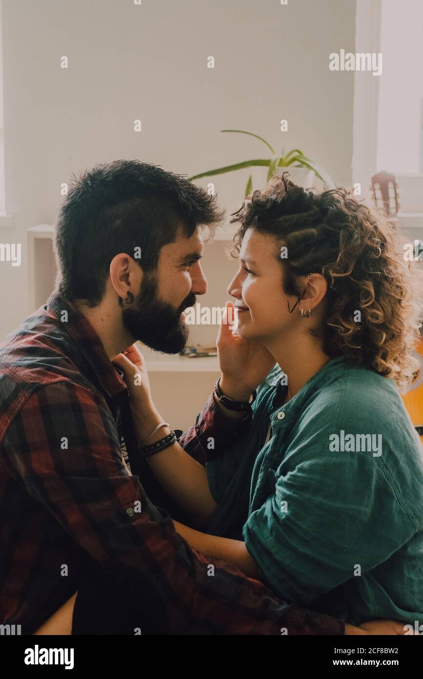 Side view of tender couple in casual clothes cuddling and smiling while ...