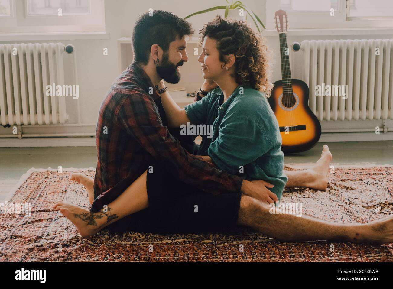 Side view of tender couple in casual clothes cuddling and smiling while ...