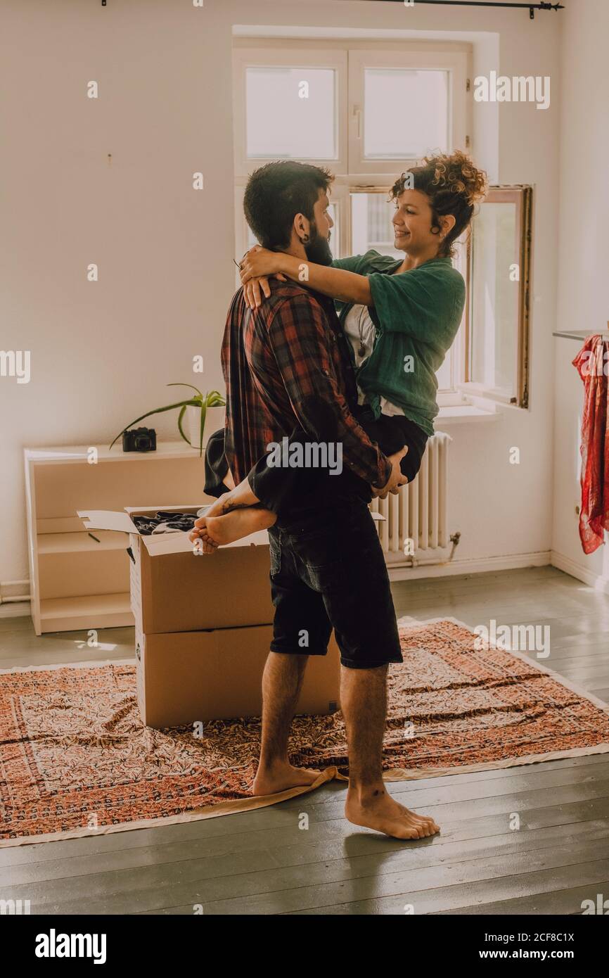 Side view of affectionate couple cuddling and front carrying while ...