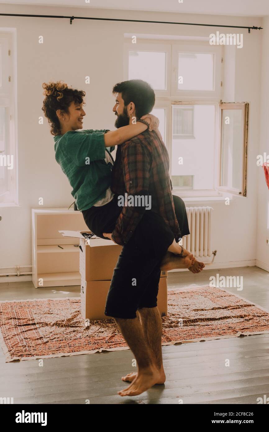 Side view of affectionate couple cuddling and front carrying while ...