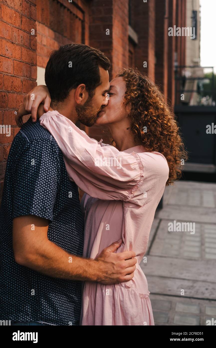 Loving couple cuddling and kissing while standing near brick building ...