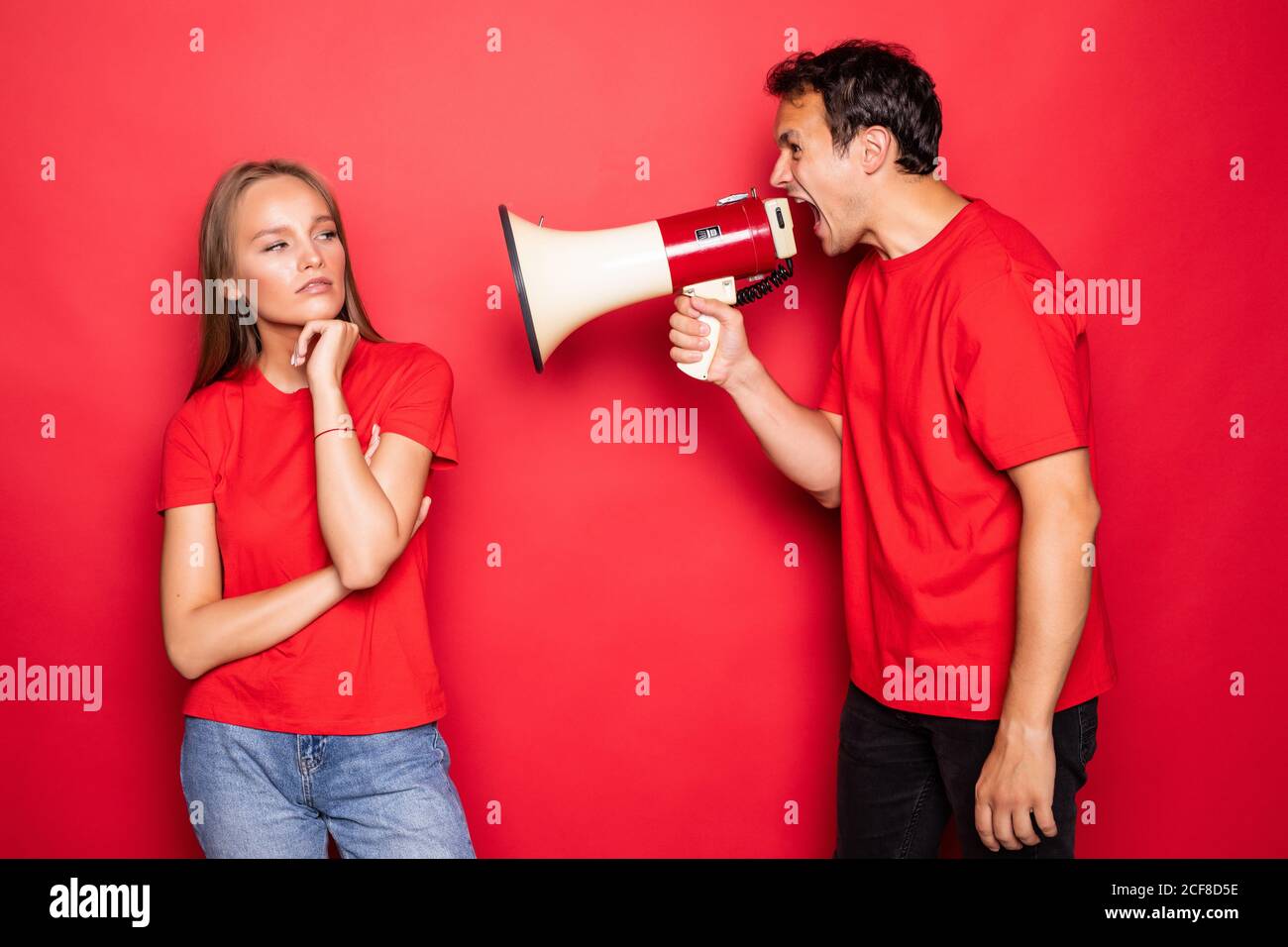 Portrait of young couple shouting with a megaphone on red background ...