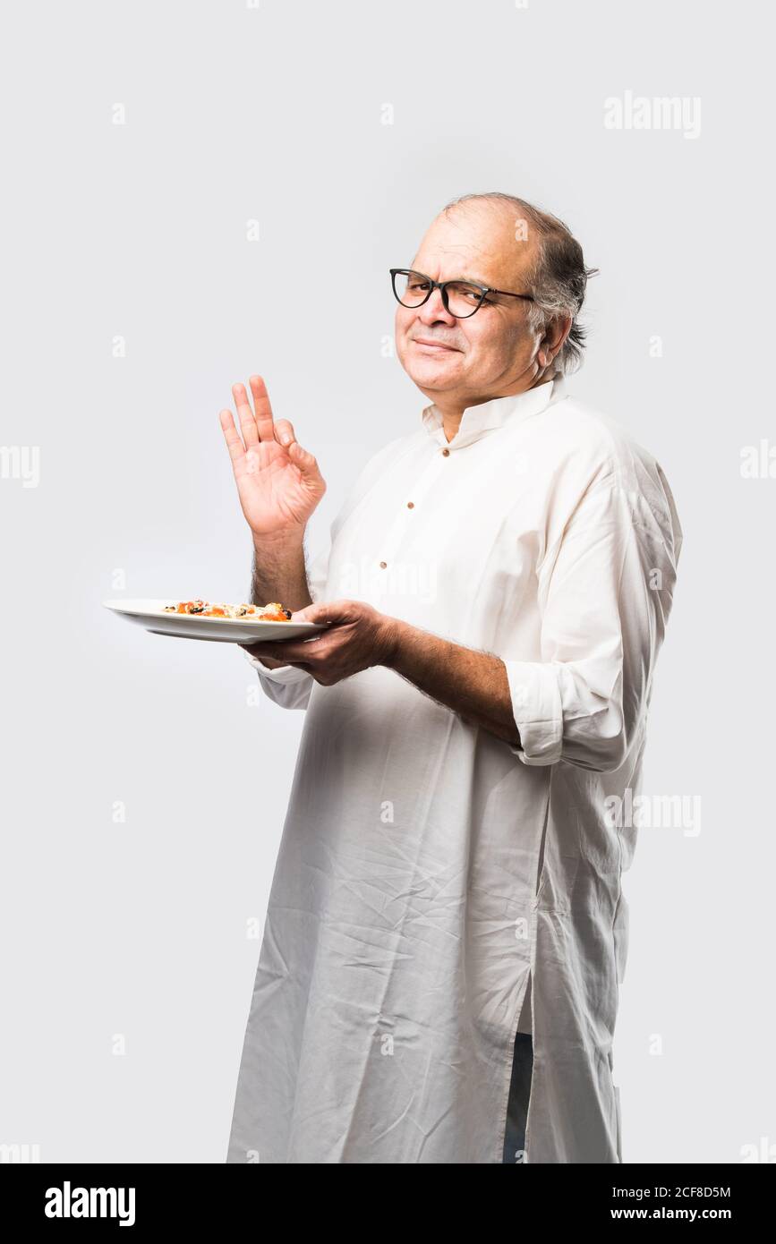Indian asian senior or old man eating pizza while standing isolated ...