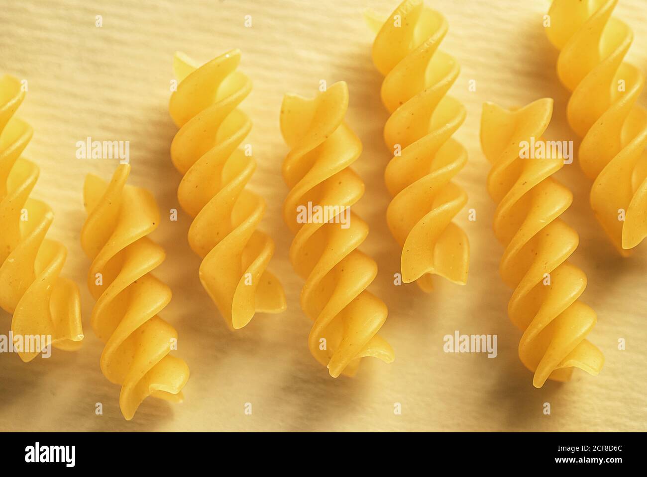 Dried spiral Italian rotini pasta in close up on a textured yellow ...