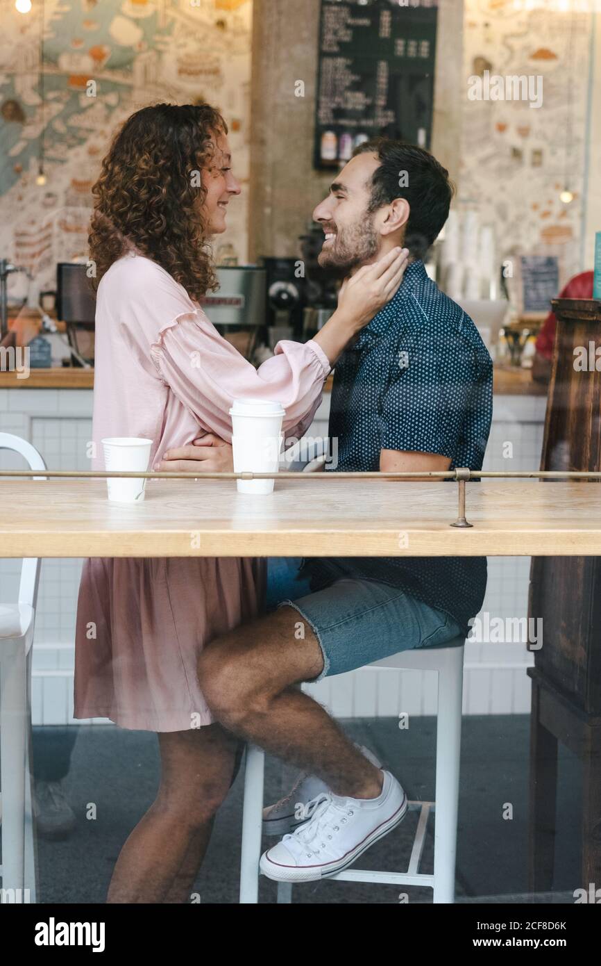 Side view of cheerful couple hugging in coffee shop drinking hot ...