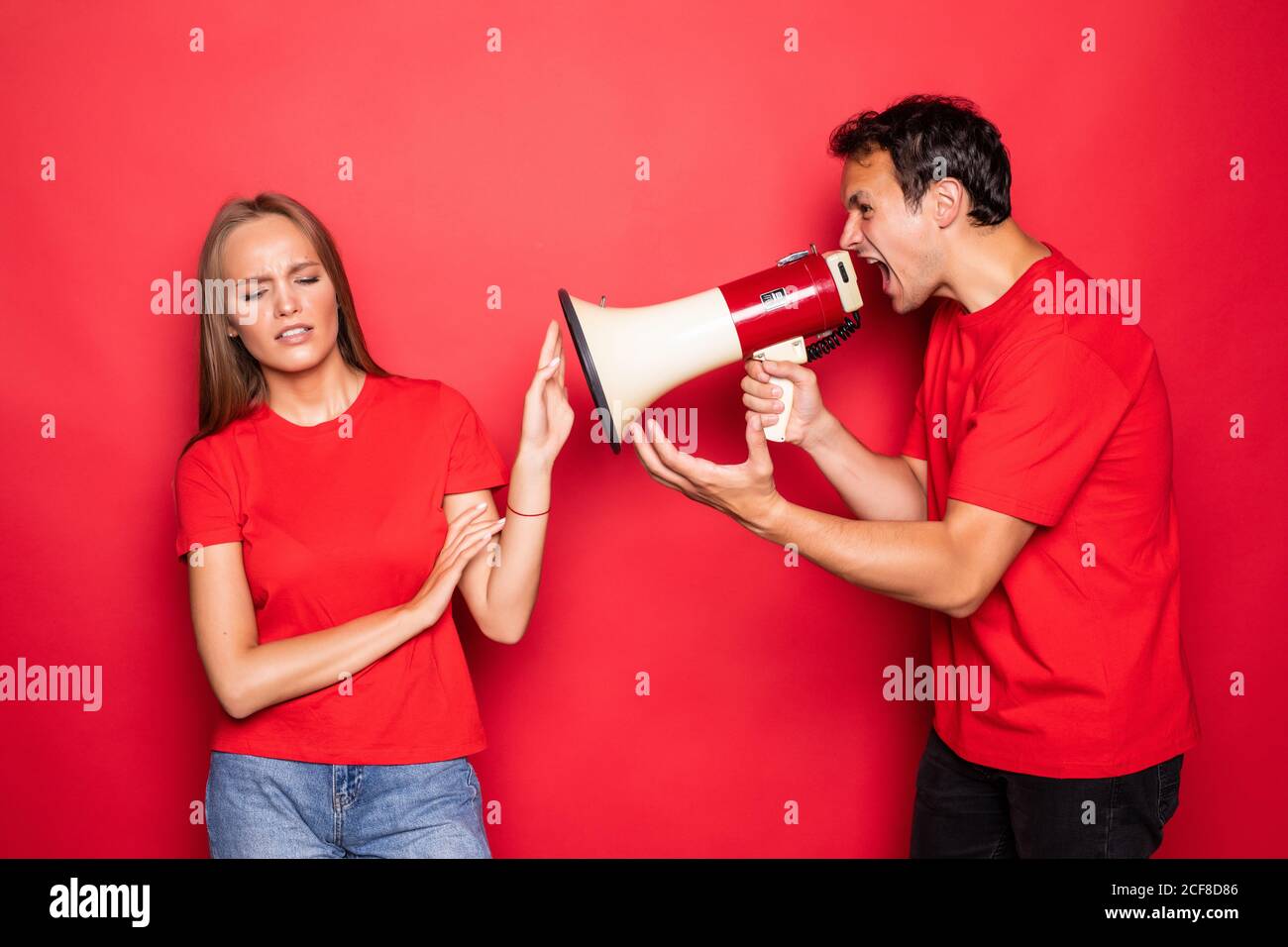 Portrait of young couple shouting with a megaphone on red background ...
