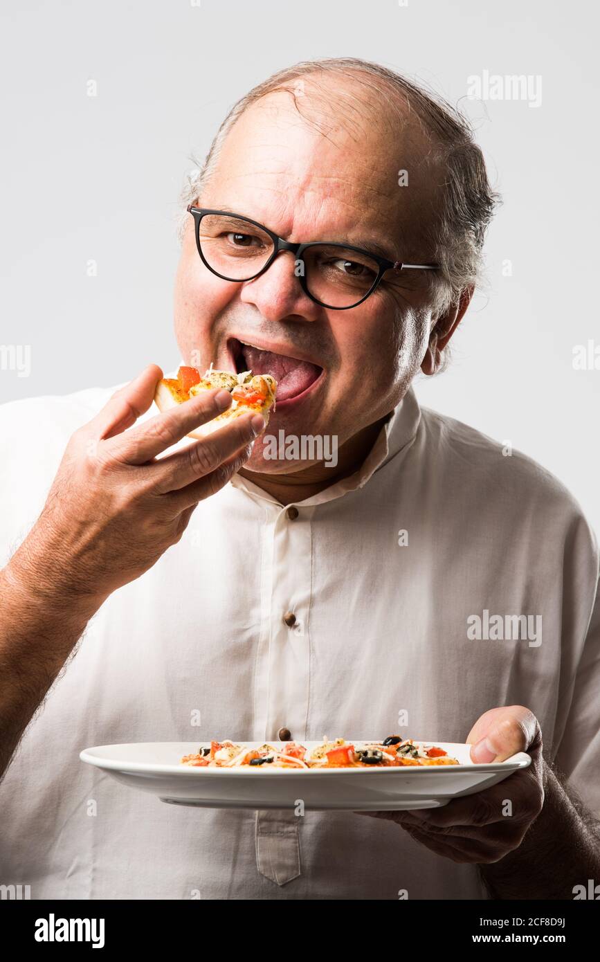 Indian asian senior or old man eating pizza while standing isolated ...