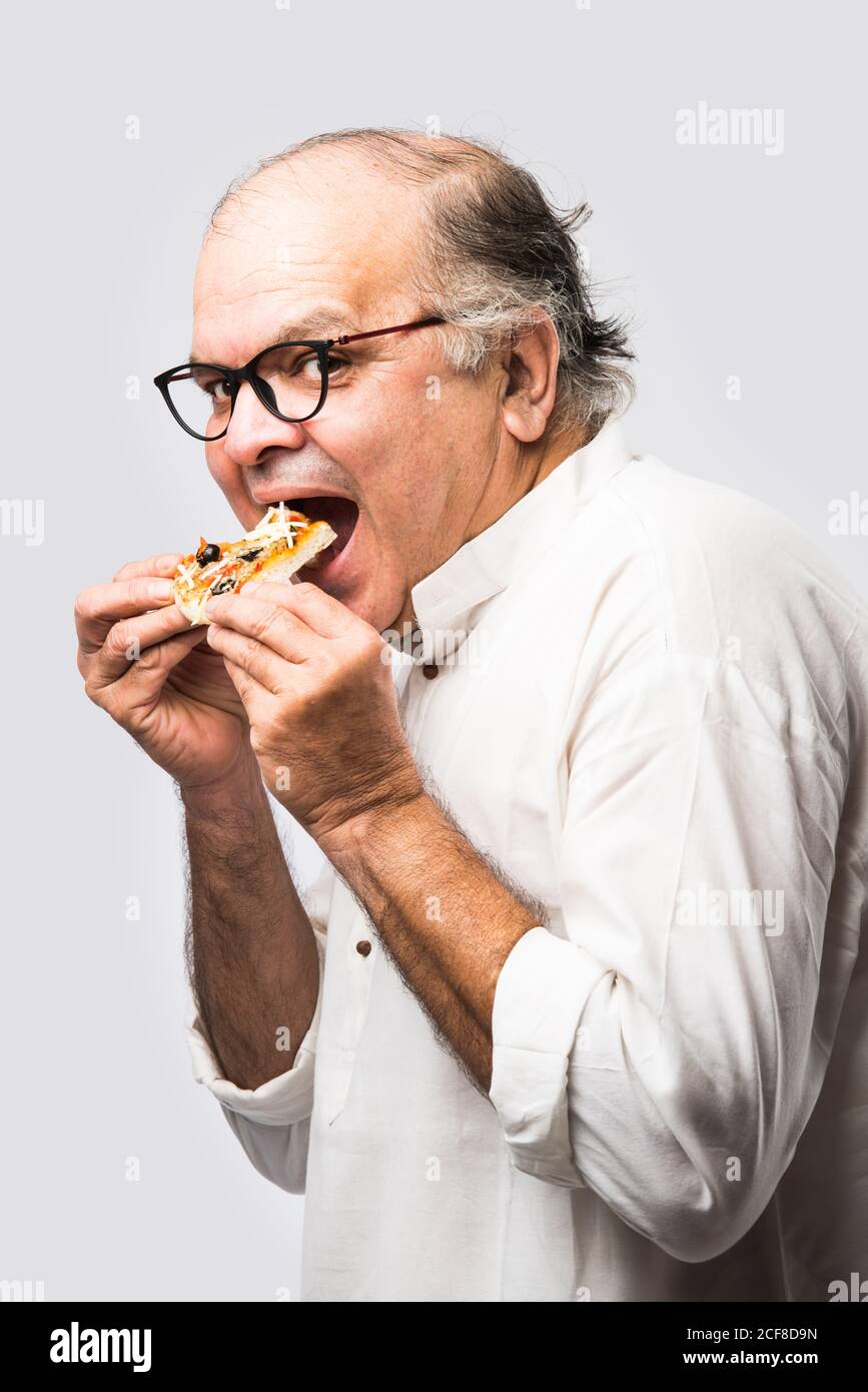 Indian asian senior or old man eating pizza while standing isolated ...