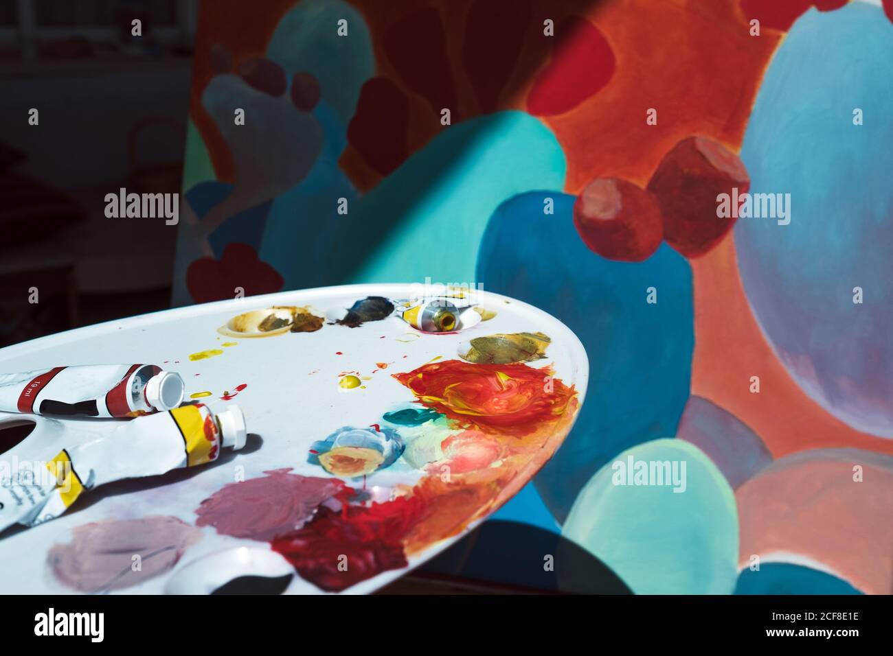 Messy palette with stains of pigment and tubes placed near easel with ...