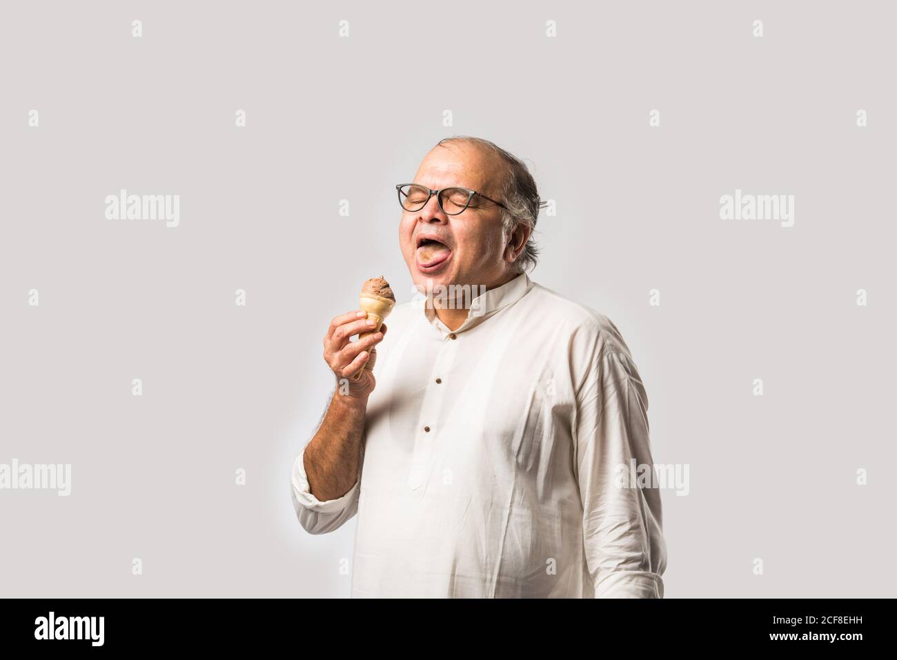 Indian Old man eating chocolate Ice cream in cone or mango candy bar ...