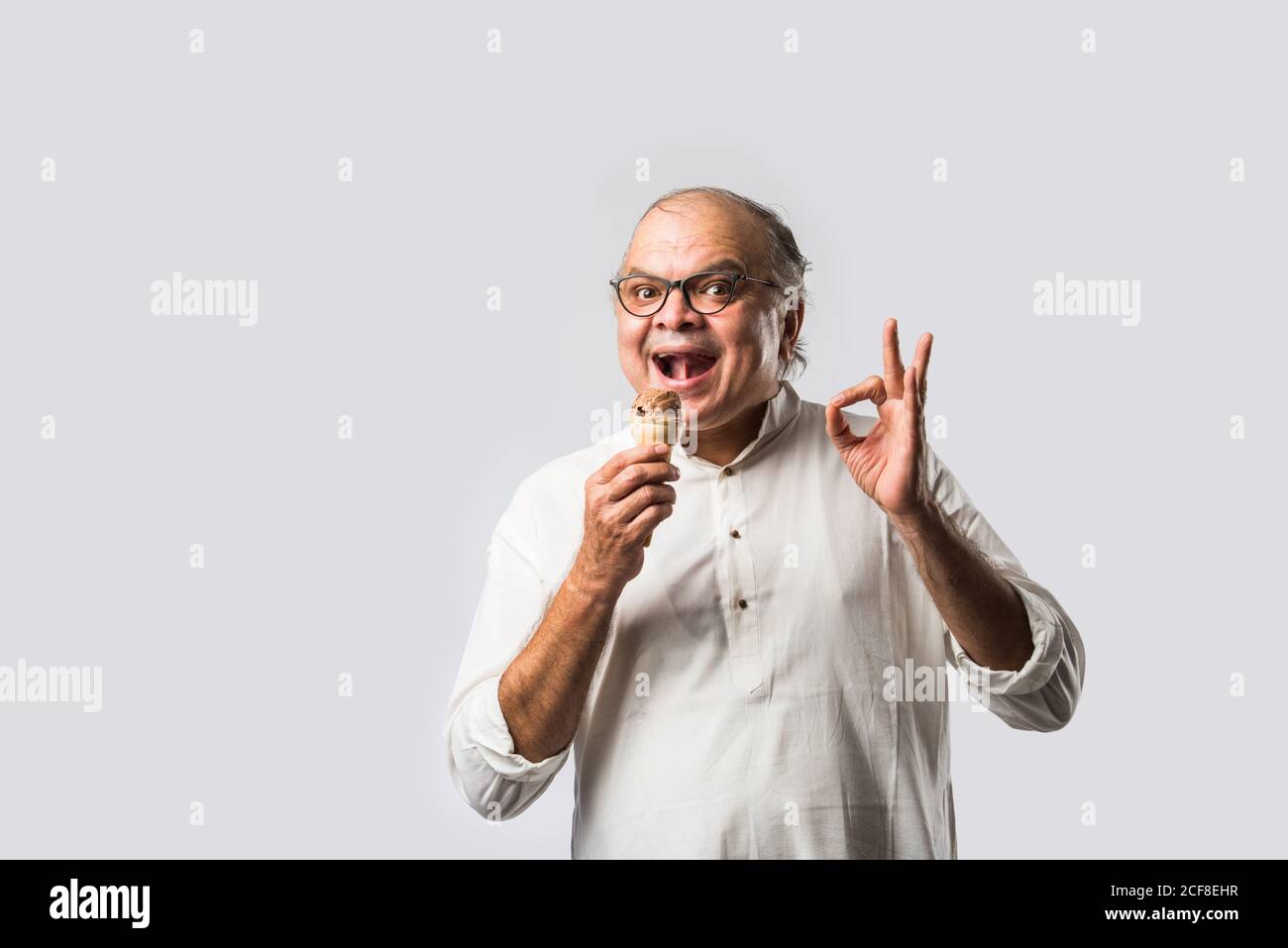 Indian Old man eating chocolate Ice cream in cone or mango candy bar ...