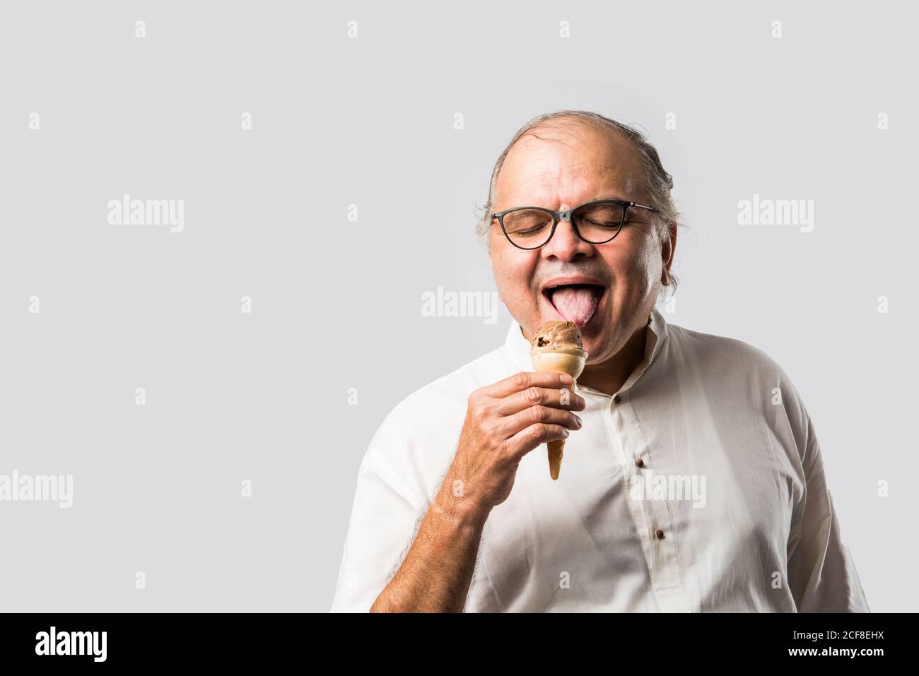 Indian Old man eating chocolate Ice cream in cone or mango candy bar ...