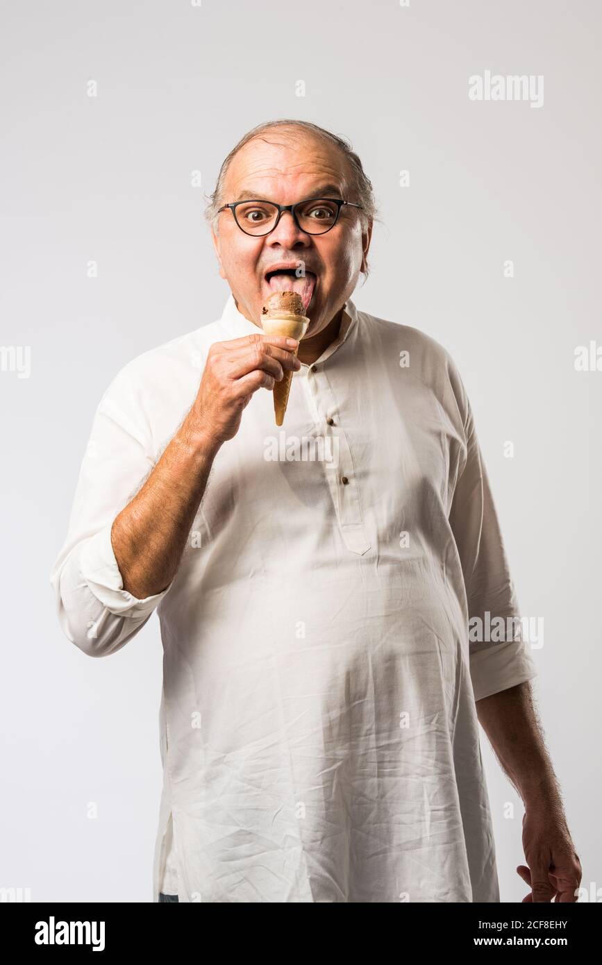 Indian Old man eating chocolate Ice cream in cone or mango candy bar ...