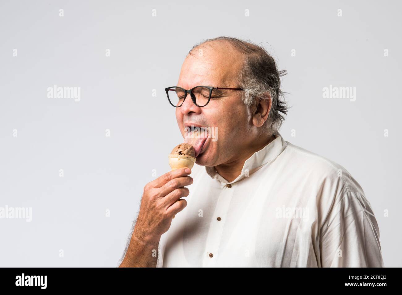 Indian Old man eating chocolate Ice cream in cone or mango candy bar ...