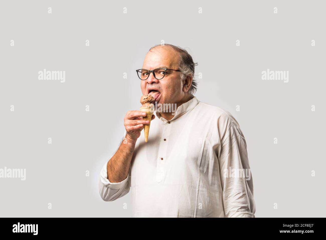Indian Old man eating chocolate Ice cream in cone or mango candy bar ...