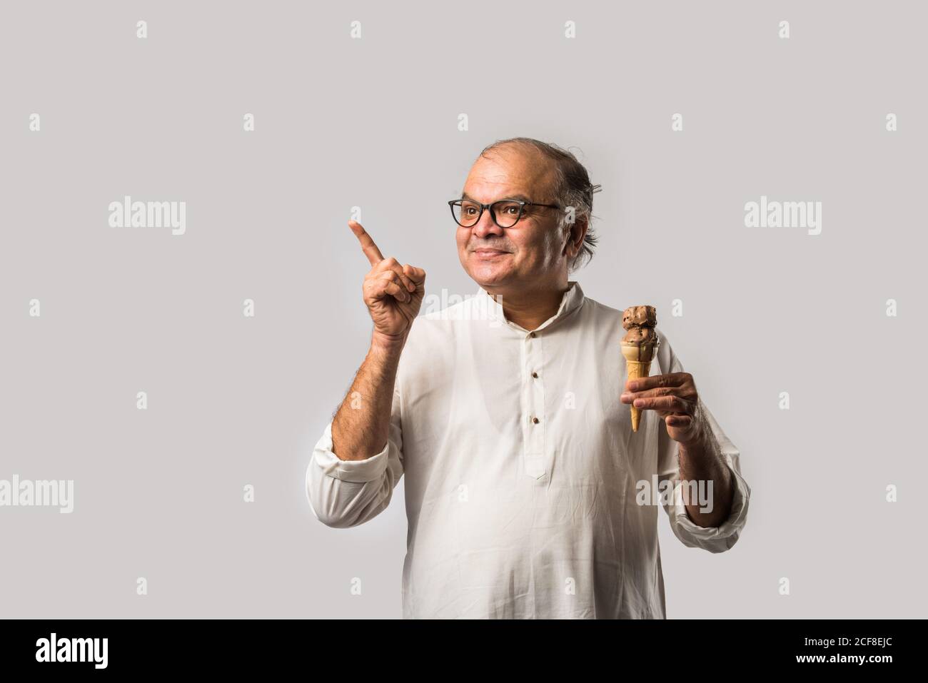 Indian Old man eating chocolate Ice cream in cone or mango candy bar ...