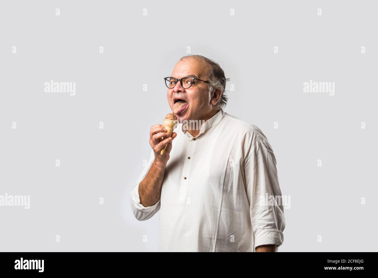 Indian Old man eating chocolate Ice cream in cone or mango candy bar ...