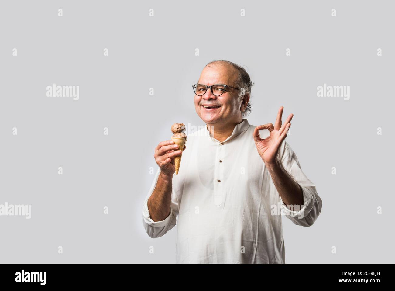 Indian Old man eating chocolate Ice cream in cone or mango candy bar ...