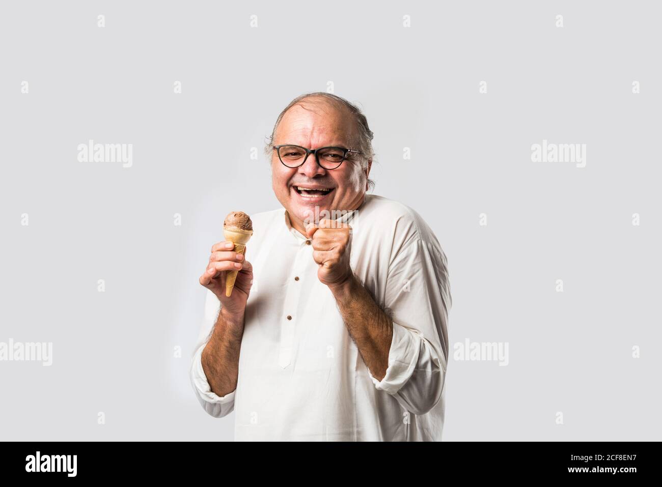 Indian Old man eating chocolate Ice cream in cone or mango candy bar ...