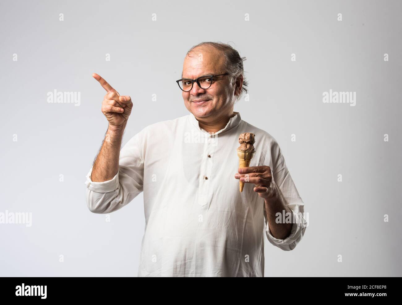 Indian Old man eating chocolate Ice cream in cone or mango candy bar ...