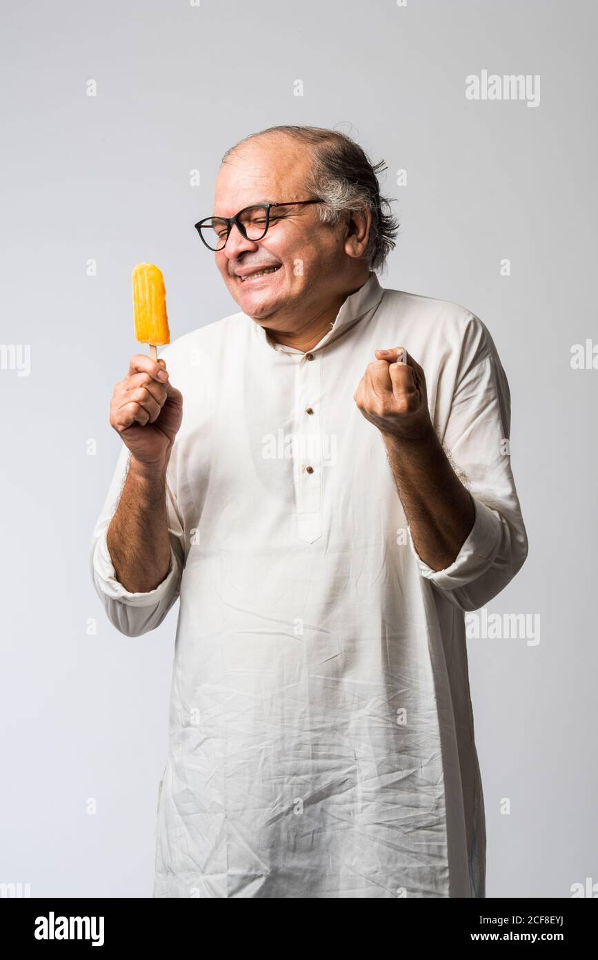 Indian Old man eating chocolate Ice cream in cone or mango candy bar ...