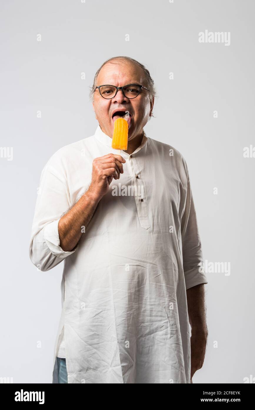 Indian Old man eating chocolate Ice cream in cone or mango candy bar ...