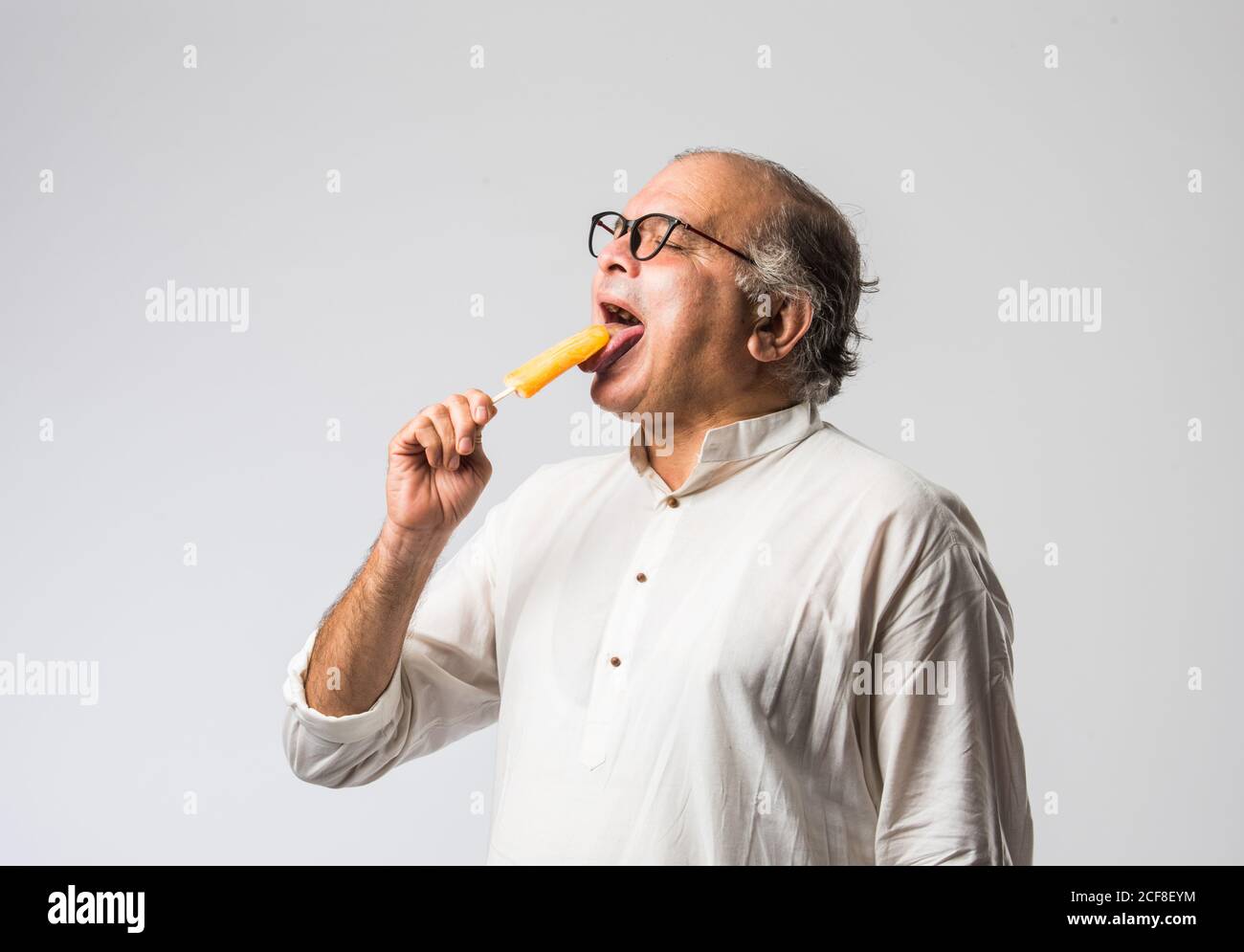Indian Old man eating chocolate Ice cream in cone or mango candy bar ...