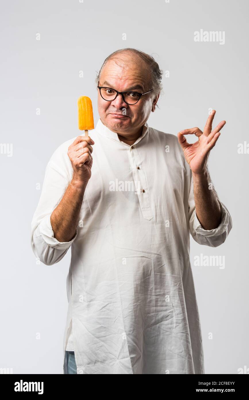 Indian Old man eating chocolate Ice cream in cone or mango candy bar ...
