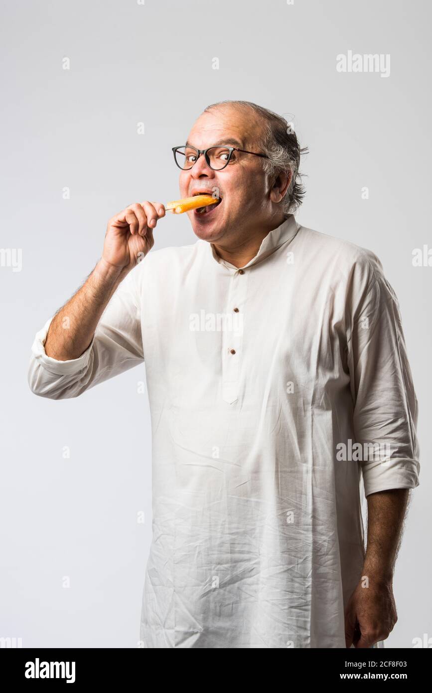 Indian Old man eating chocolate Ice cream in cone or mango candy bar ...
