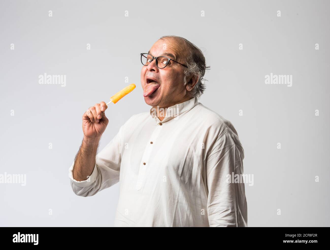 Indian Old man eating chocolate Ice cream in cone or mango candy bar ...