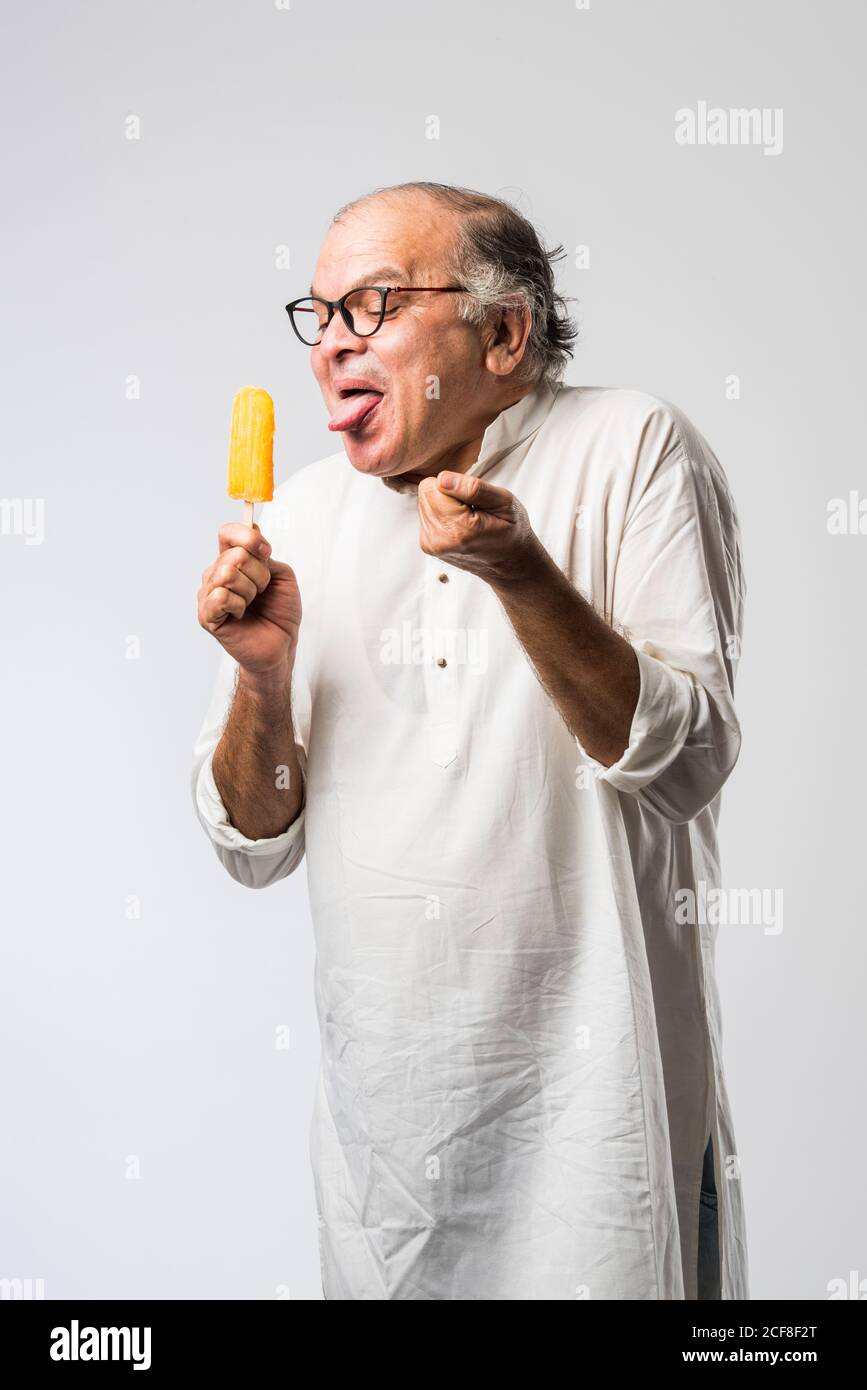 Indian Old man eating chocolate Ice cream in cone or mango candy bar ...