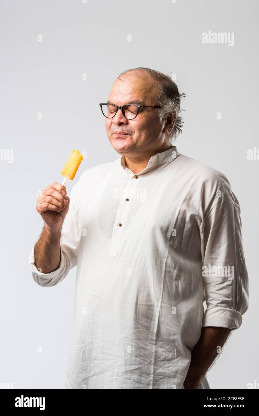 Indian Old man eating chocolate Ice cream in cone or mango candy bar ...