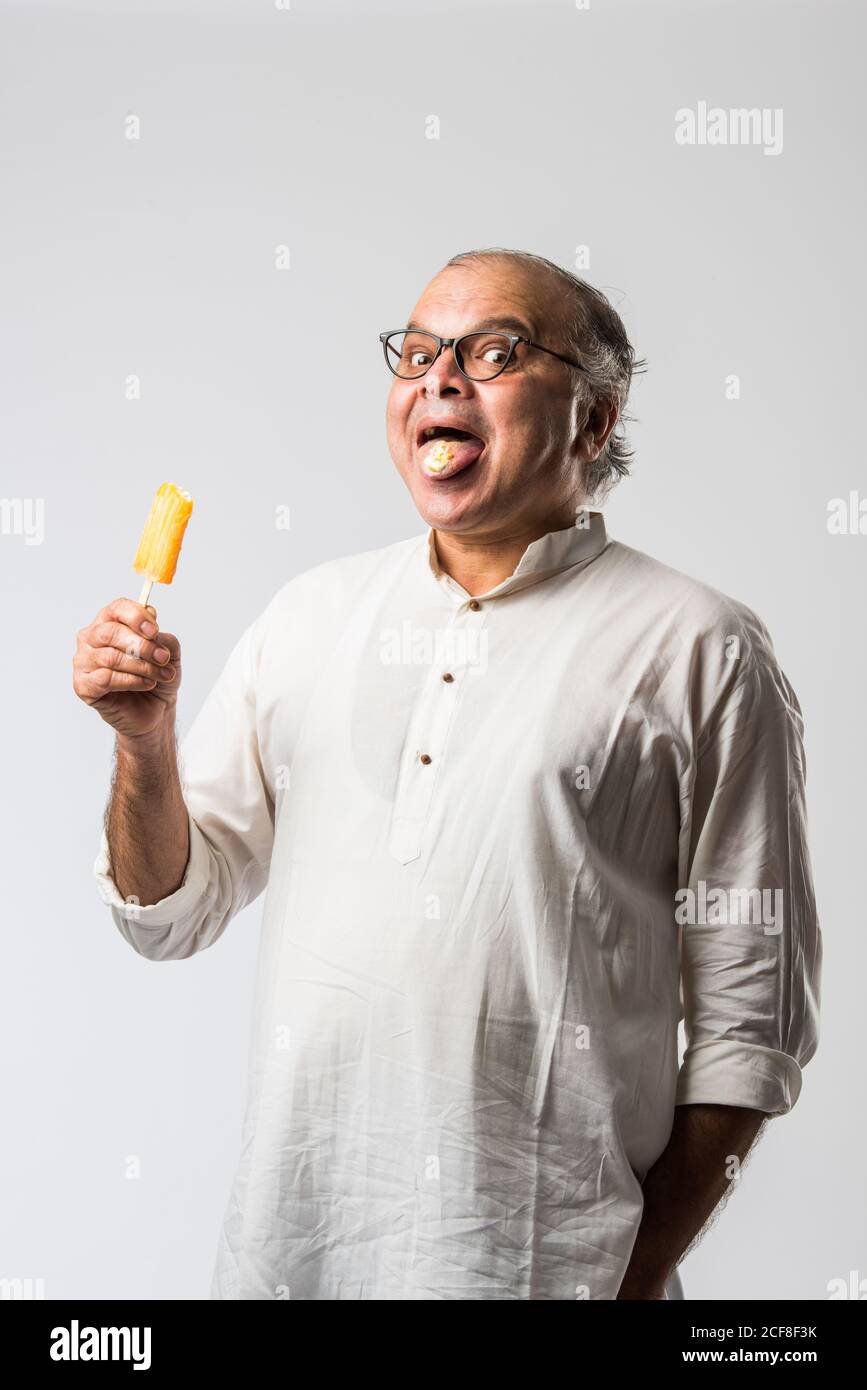 Indian Old man eating chocolate Ice cream in cone or mango candy bar ...