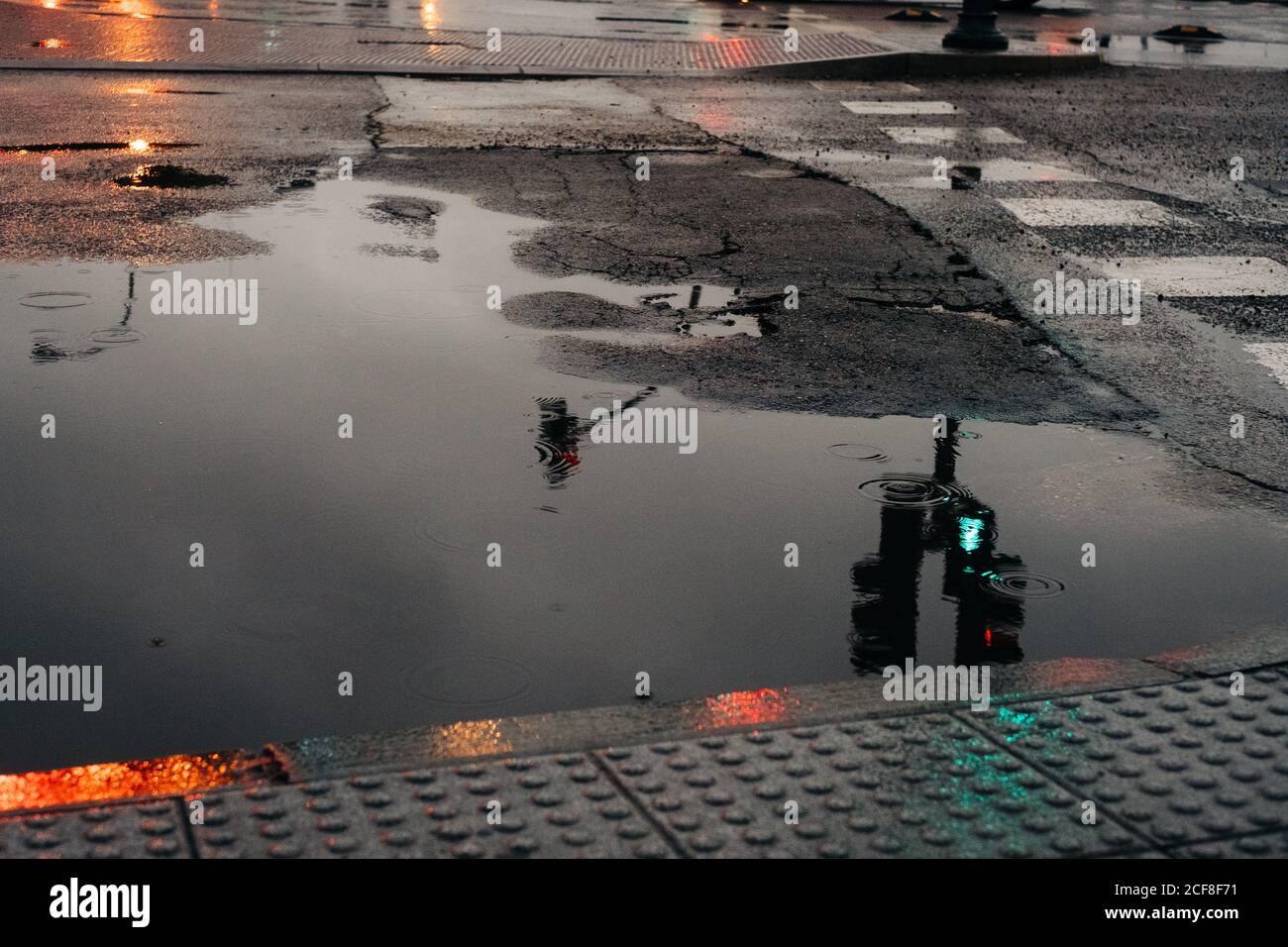 Reflection of glowing light in puddle of water in rainy evening on city ...