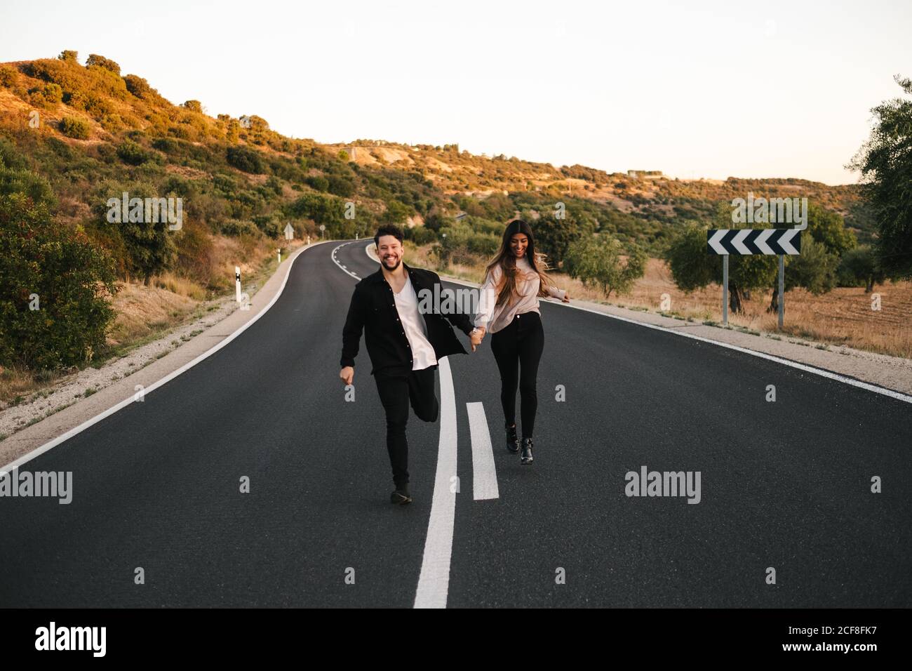 Stylish boyfriend and girlfriend running along empty roadway in ...