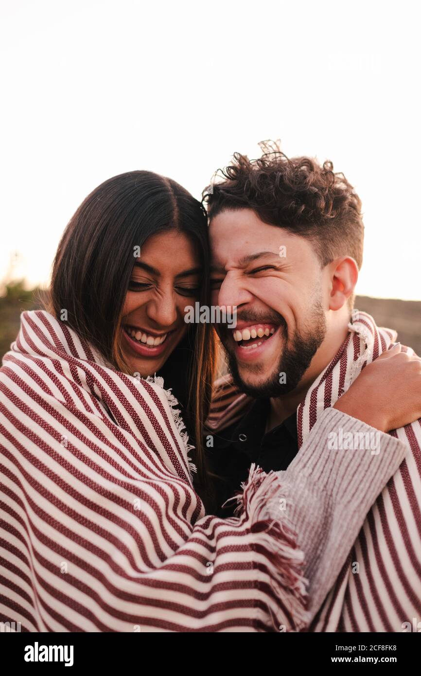 Delighted ethnic girlfriend and boyfriend embracing while covering with ...